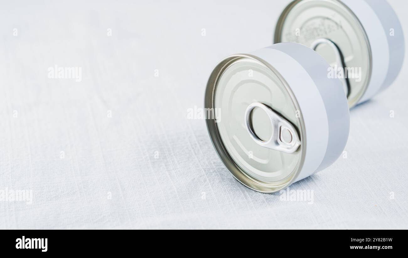 Two aluminum cans with pull-tab lids placed on a textured white surface ...