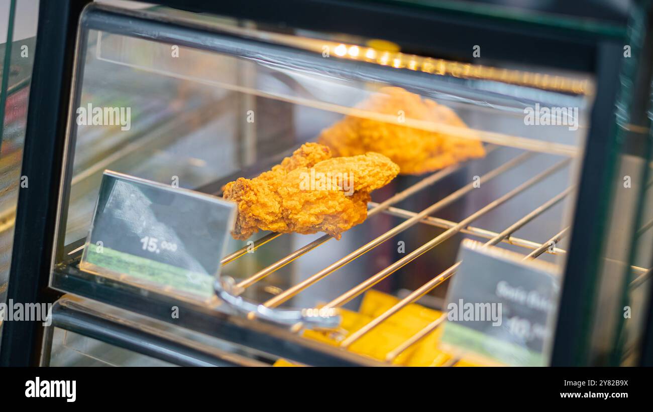 A close-up view of fried chicken pieces displayed in a glass showcase ...