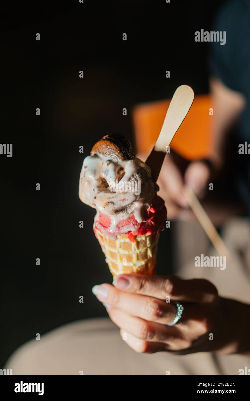 A close-up of a hand holding an ice cream cone with two scoops: one ...