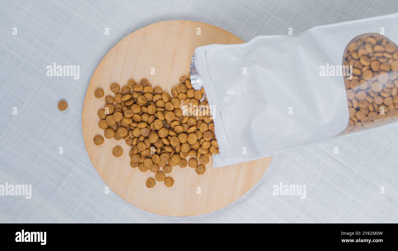 A bag of pet food being poured onto a wooden cutting board. The kibble ...
