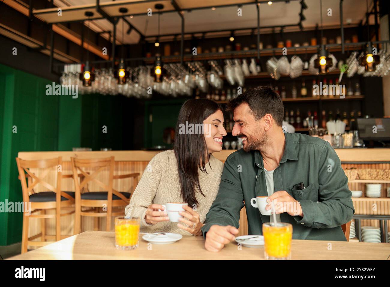 Couple shares a joyful moment at a stylish café, sipping coffee and ...