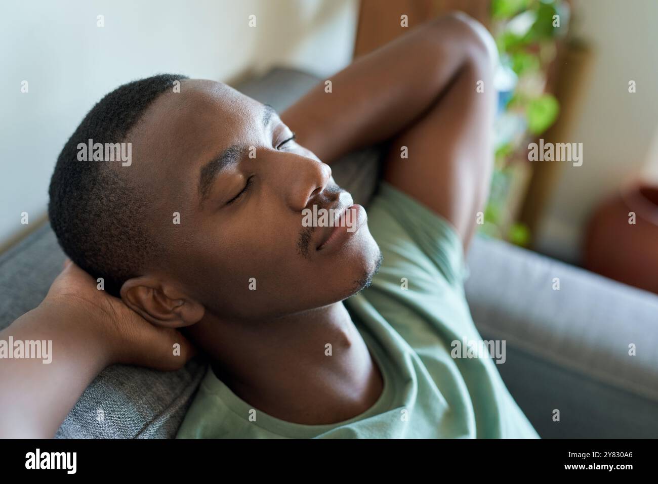 Closeup of a young African man sitting alone on his living room sofa ...