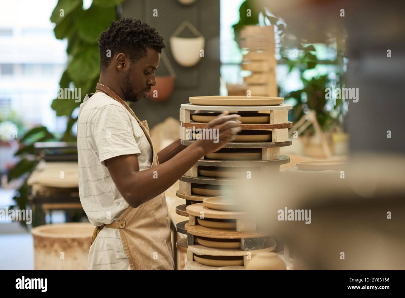Young male African pottery maker drying newly made plates on racks in a ...