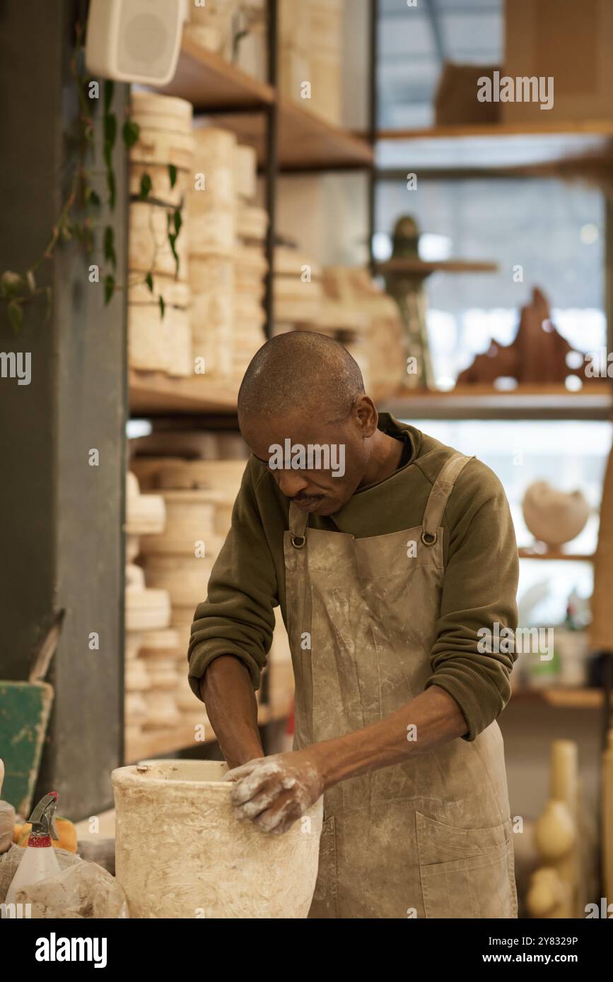African potter sanding a clay mold while working at a bench in a large ...