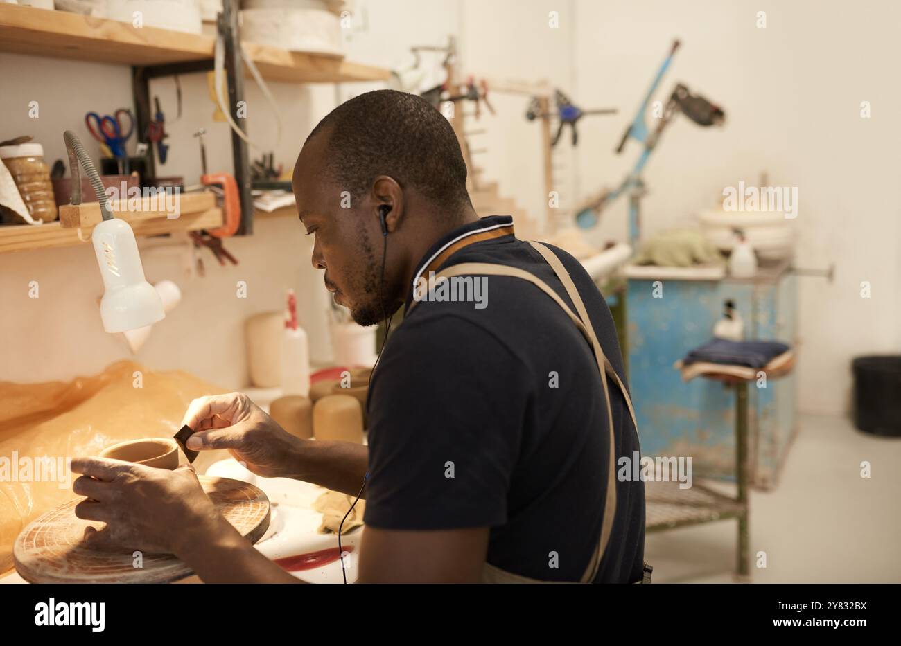 African ceramist working on a clay bowl while sitting at a bench in a ...