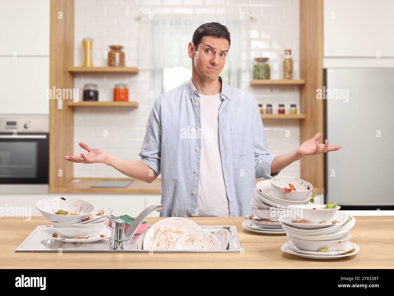 Angry man with a pile of dirty dishes in a kitchen sink on a wooden ...