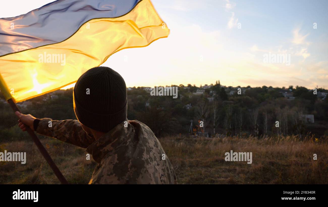Young man in military uniform waving flag of Ukraine against beautiful ...