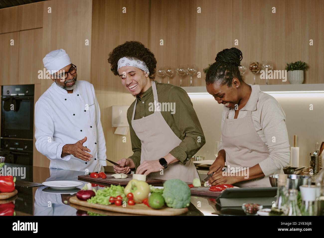 Indian chef telling jokes during work tie, his cooks laughing while cooking in modern kitchen of ...