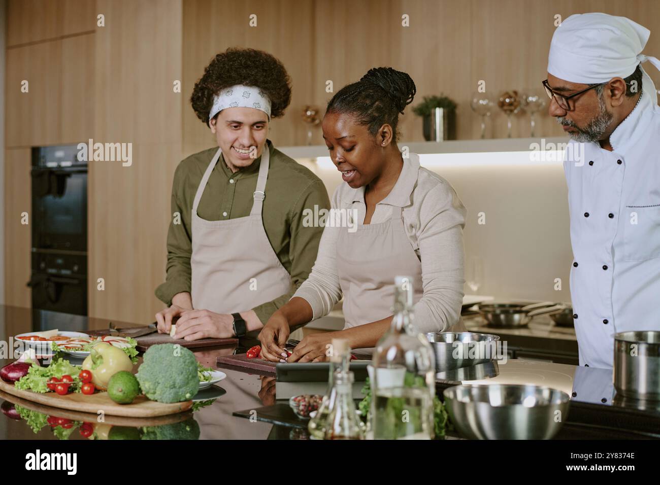 Young male sous chef helping African American female cook with cutting ...