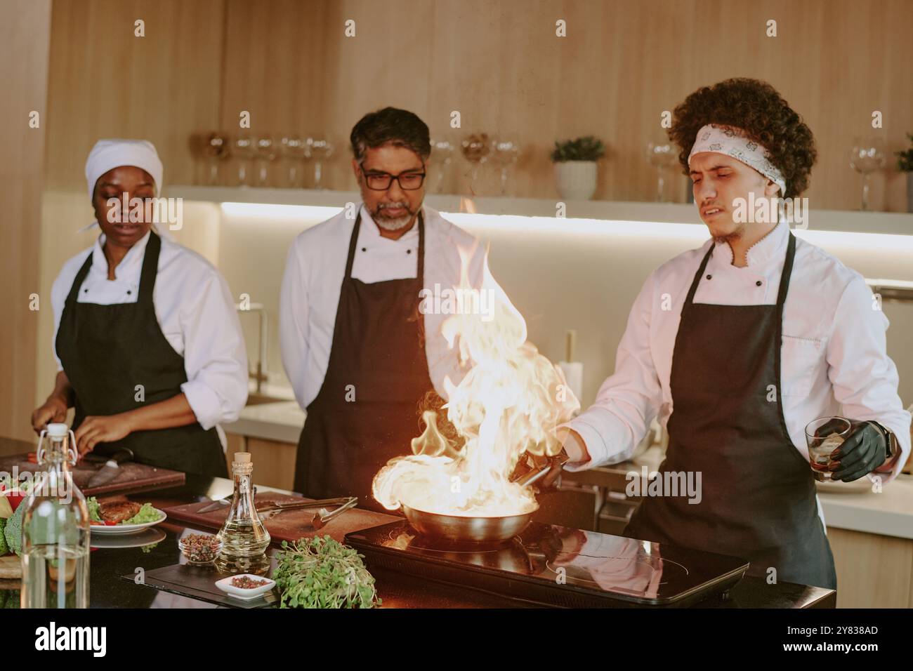 Curly Haired sous chef frying flambe steak while chef and female ...