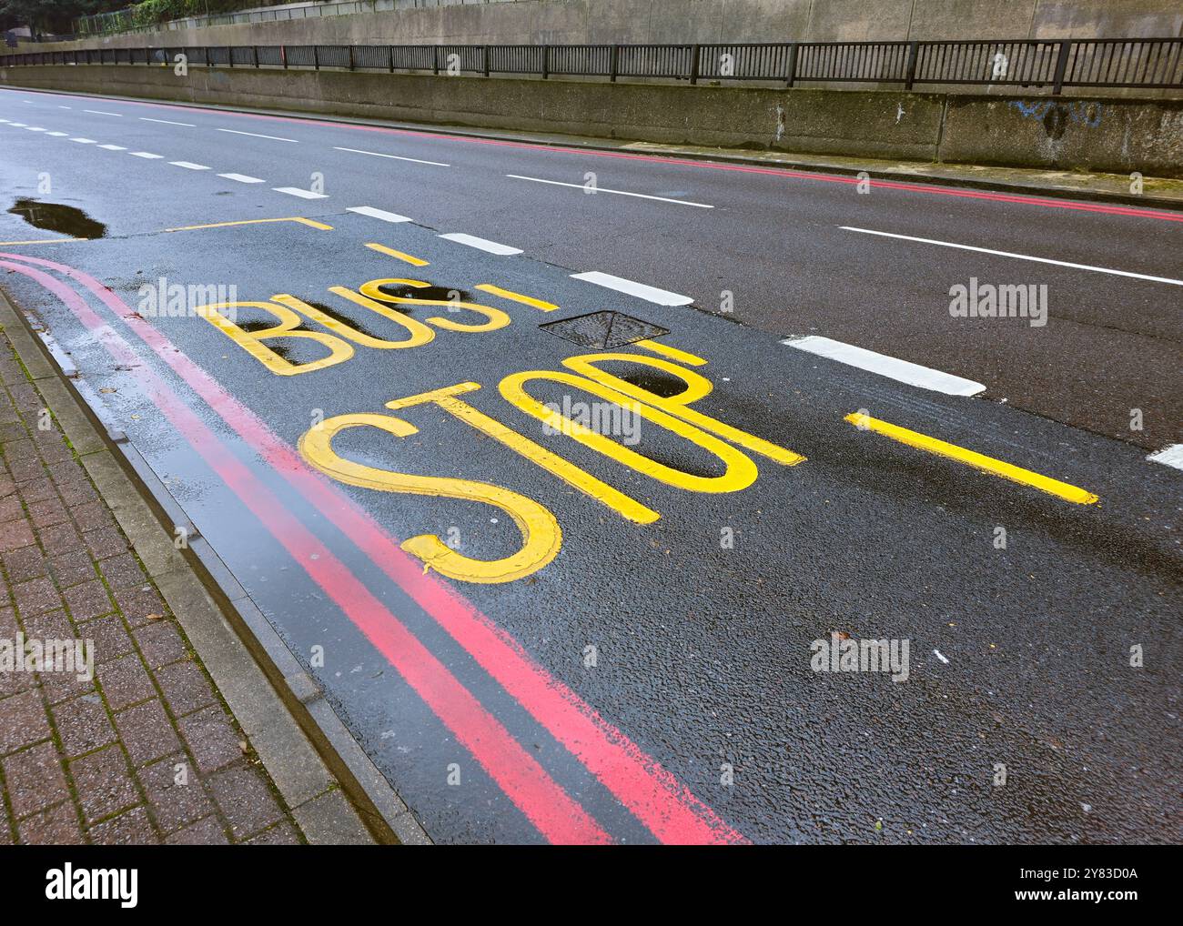 Yellow bus stop sign painted on the road by a bus stop with a wet ...