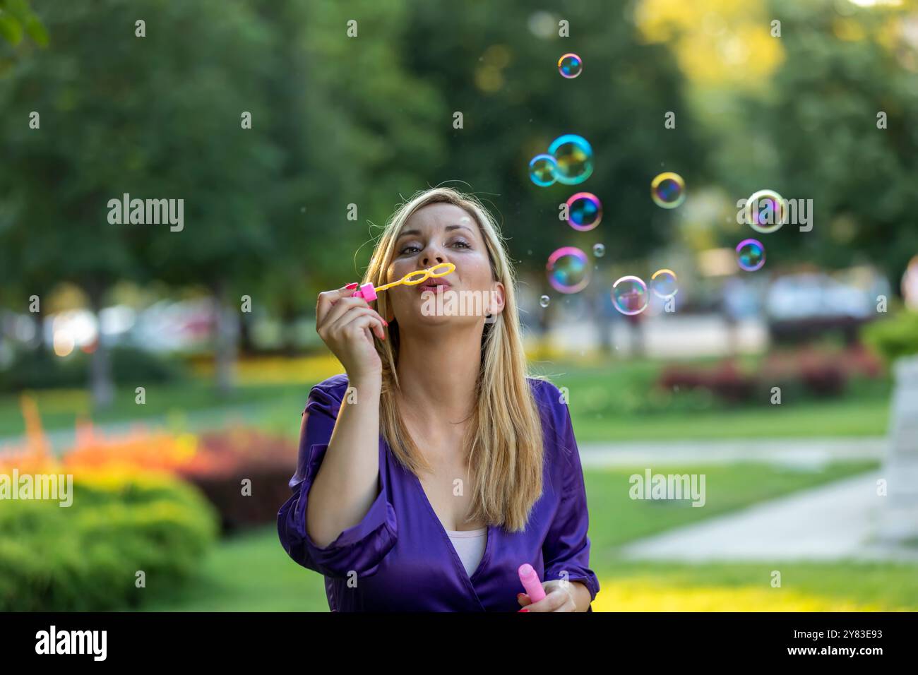 Beautiful Woman with Long Hair and Violet Dress is Walking in Public Park and Holding and ...