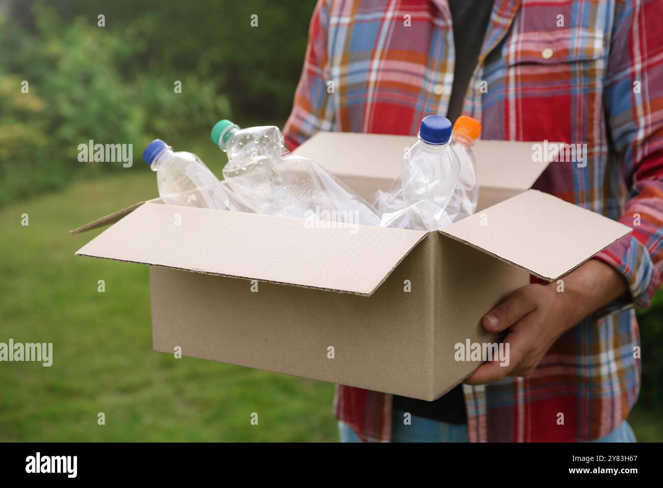 Recycling. Man holding cardboard box with plastic bottles outdoors ...