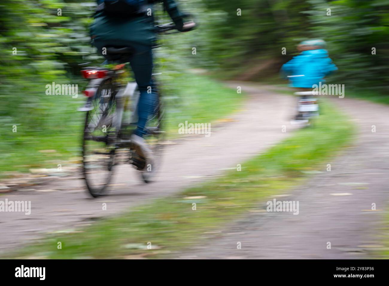 Adult and child riding bicycles in motion blur on a country lane ...