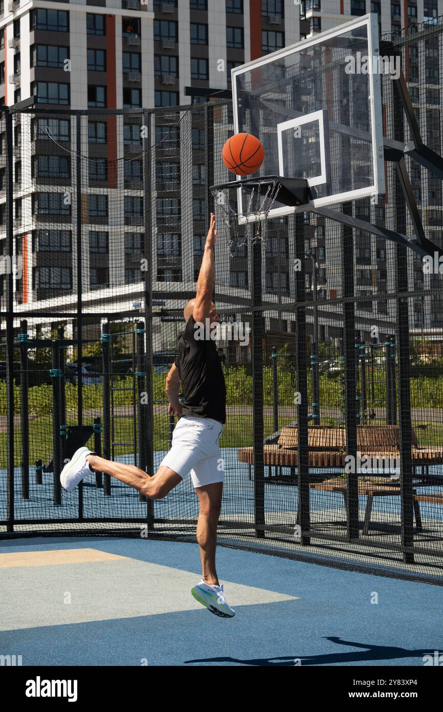 Sporty man throw ball into basketball hoop on sports court at courtyard ...