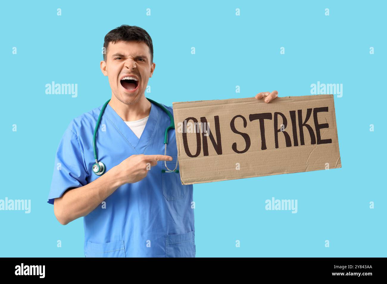 Protesting male doctor pointing at placard with text ON STRIKE against ...