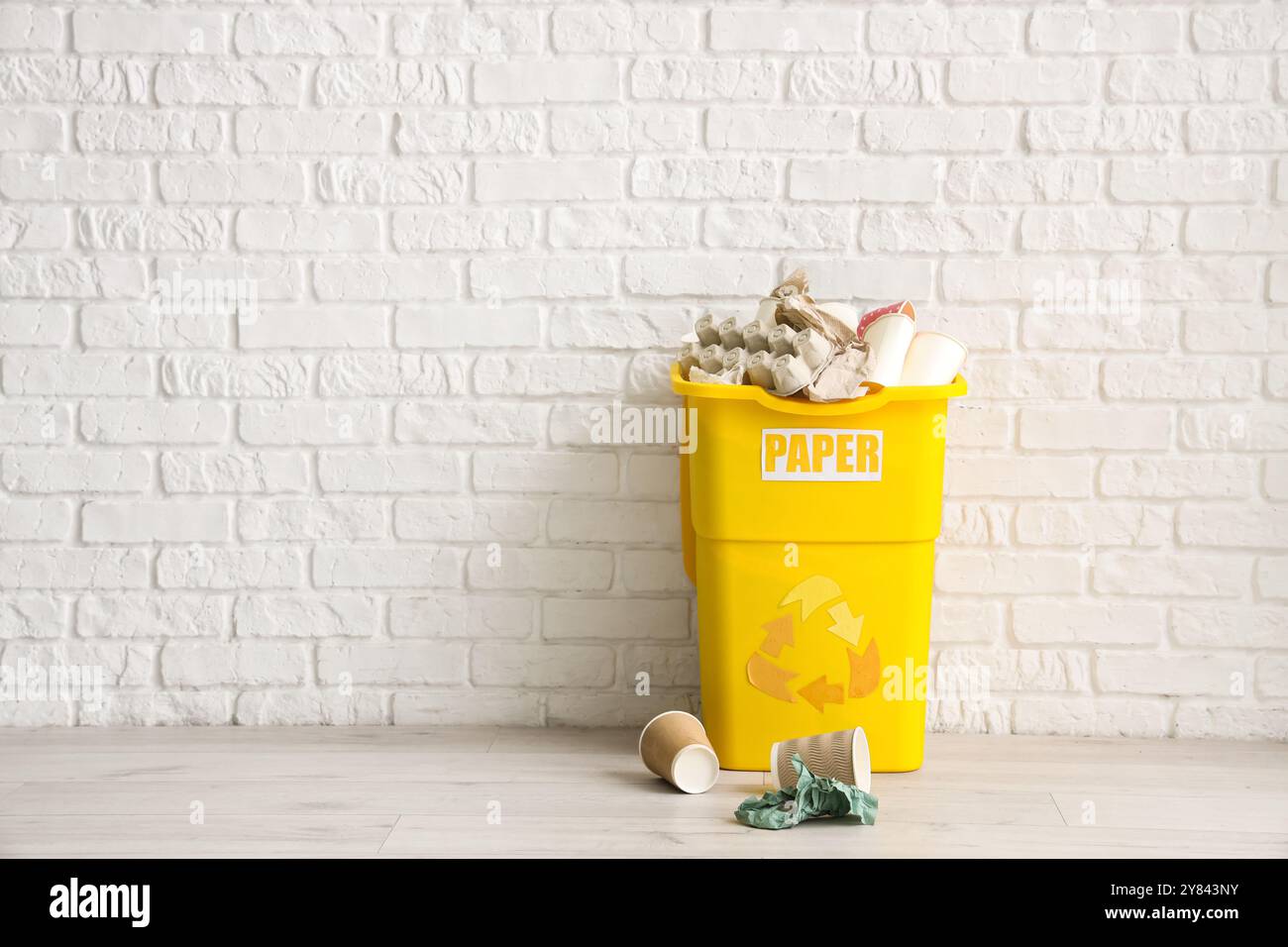 Full trash bin with PAPER sign near white brick wall. Recycling concept ...