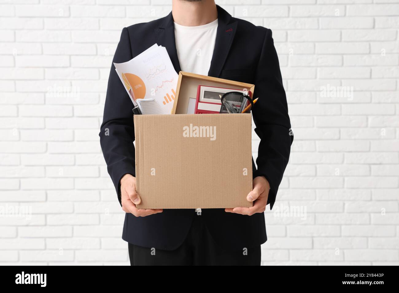 Fired young businessman holding box with personal stuff on white brick ...
