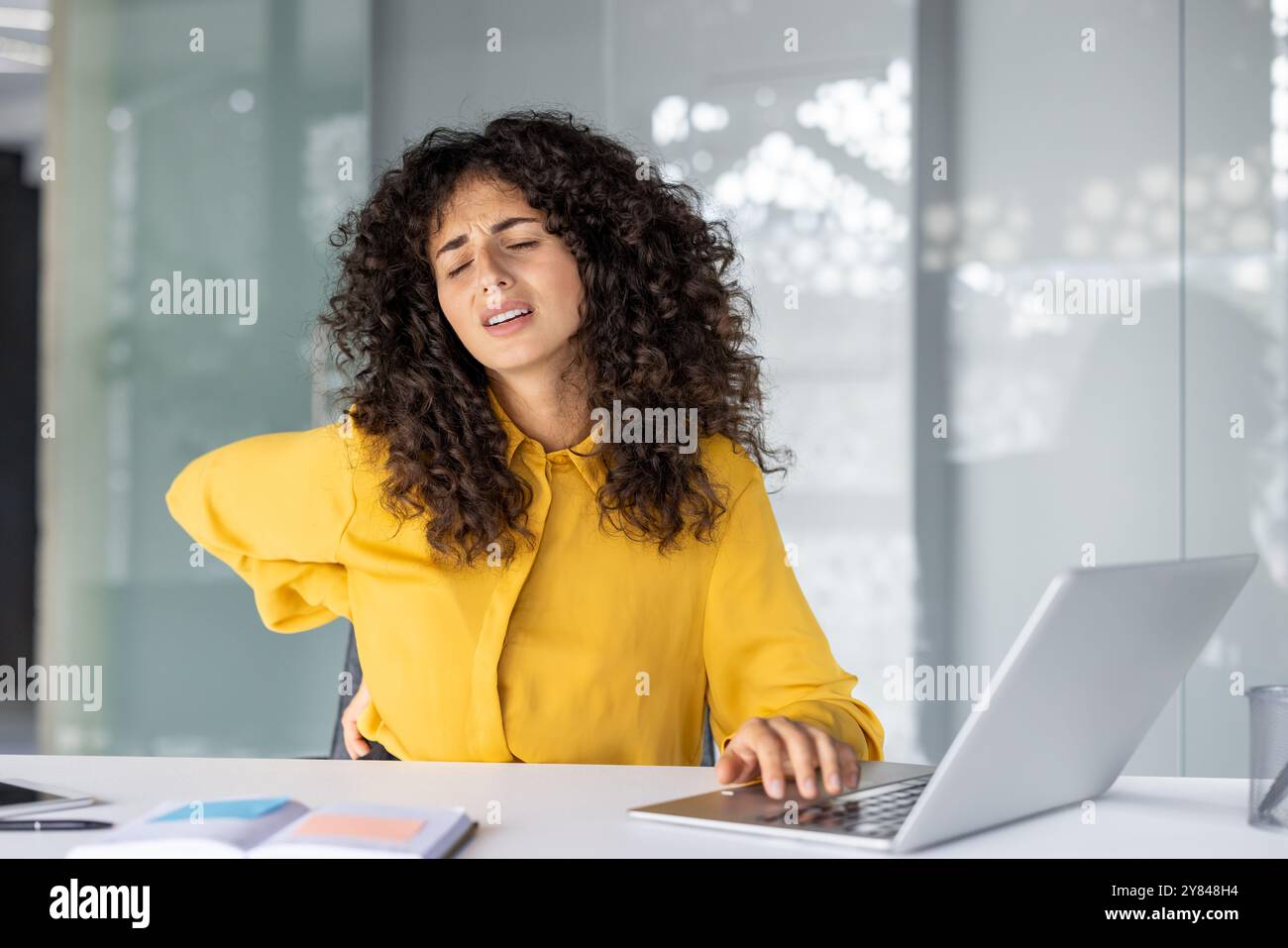Hispanic businesswoman feeling discomfort from back pain seated at desk ...