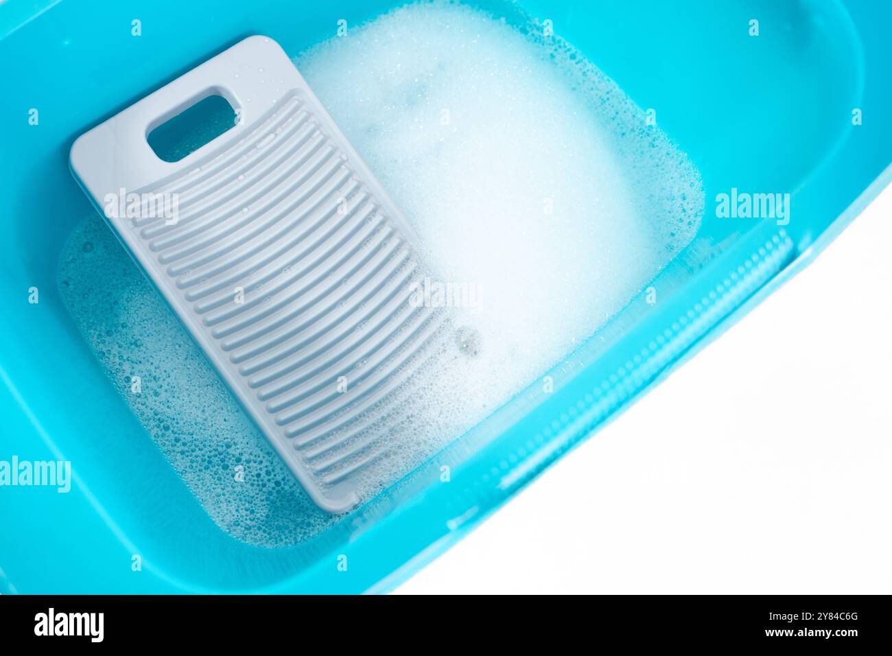 Blue plastic basin filled with soapy water and portable mini washboard ...