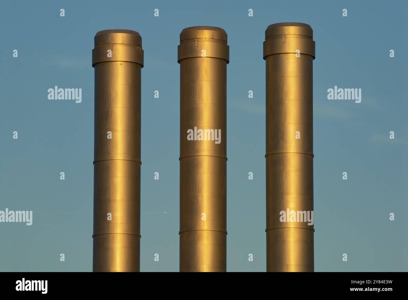 Three golden industrial chimneys in front of a clear blue sky ...