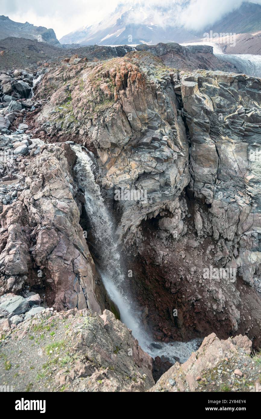 A cascading waterfall plunges down a rocky cliff, surrounded by a ...