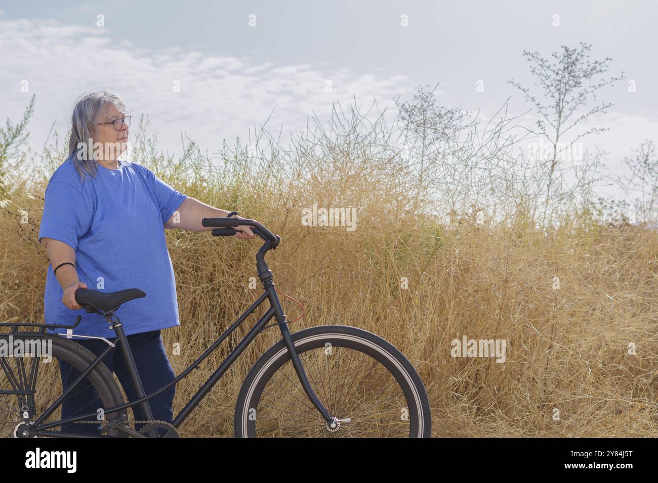 Overweight woman, seen in profile, riding a bicycle on a path covered ...