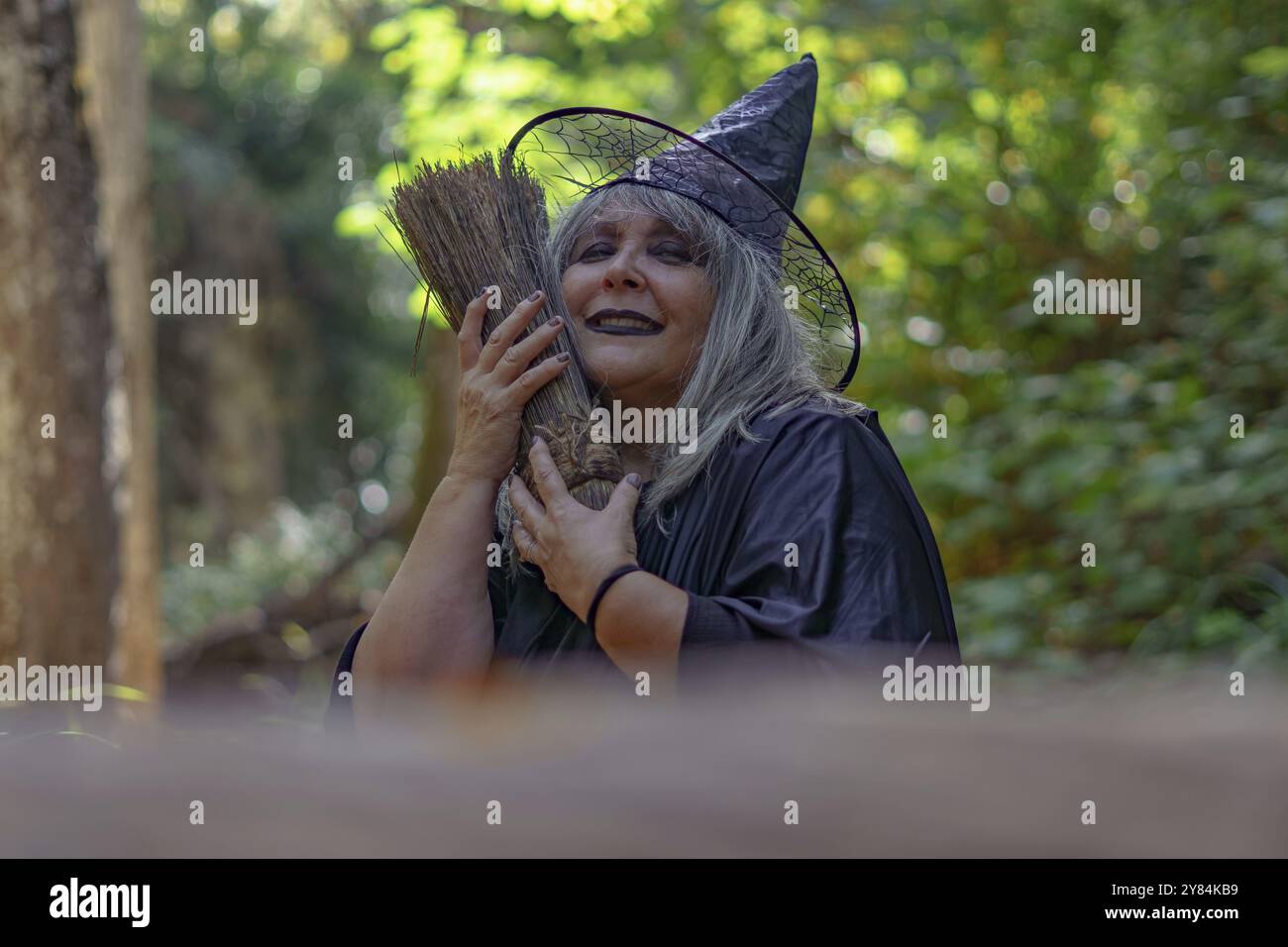 Old witch with white hair and hat smiling hugging her broomstick Stock ...