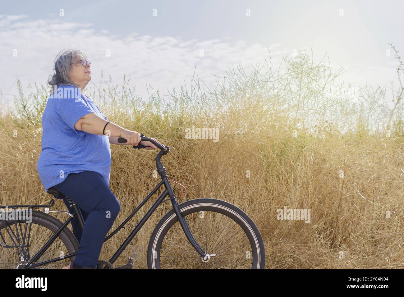 An older woman with white hair, obese, seen in profile riding a bicycle ...