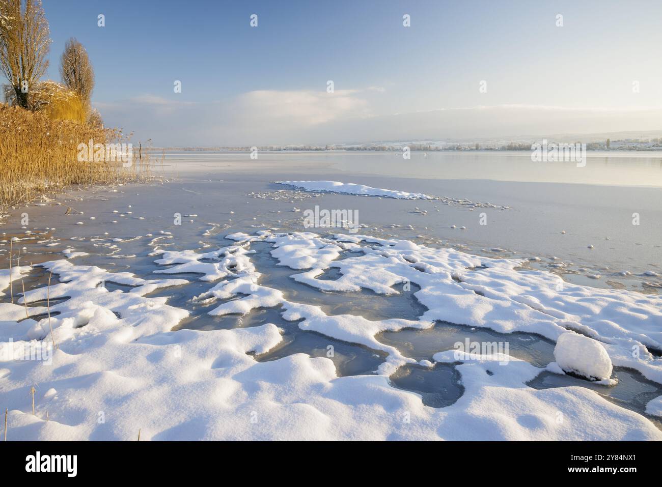 Snowy shore landscape with partially frozen lake and bright sky ...