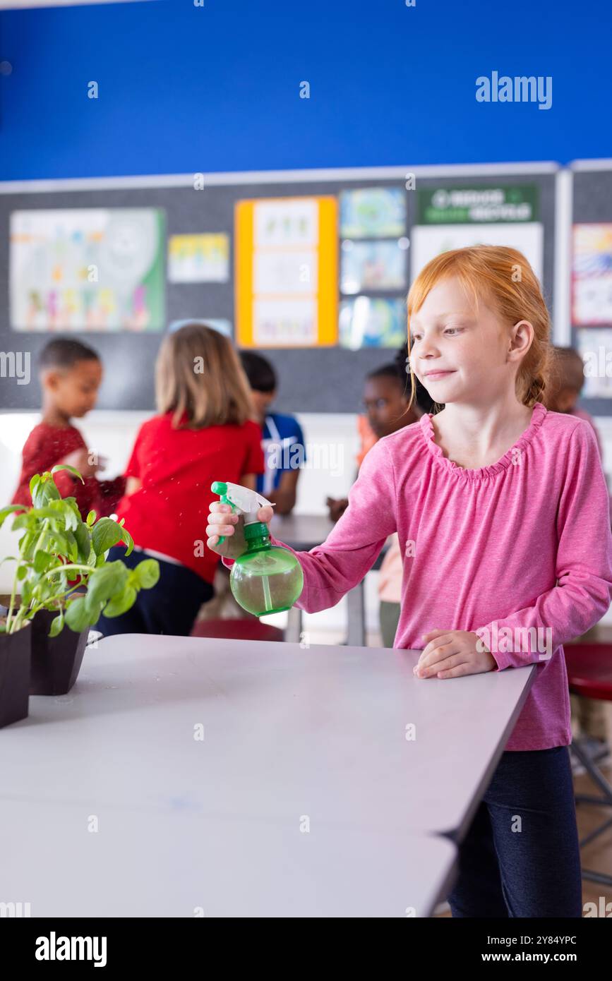 In school, girl watering plants with spray bottle in classroom, smiling ...