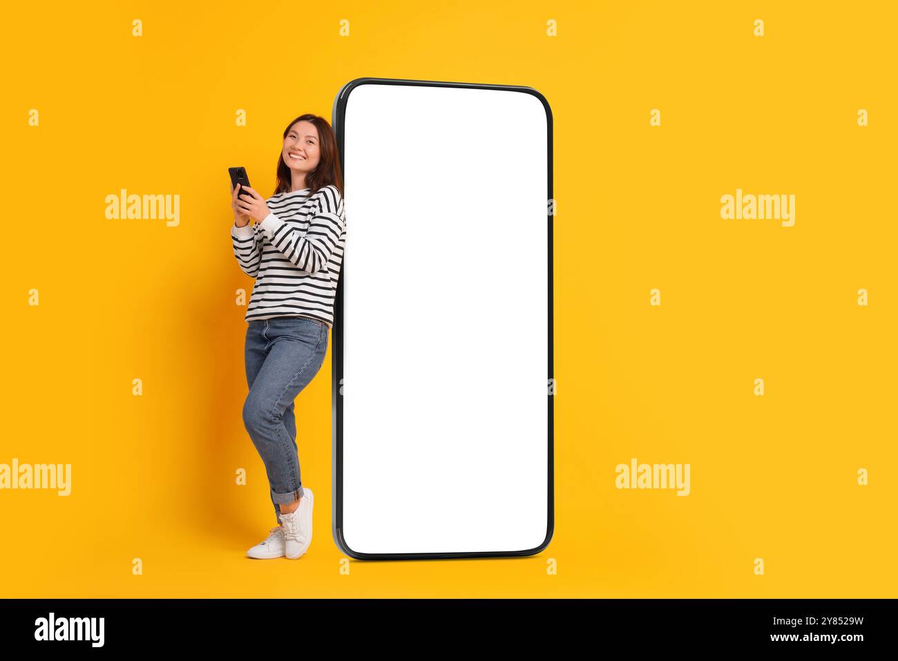 Happy smiling woman with smartphone standing near big mobile phone with ...