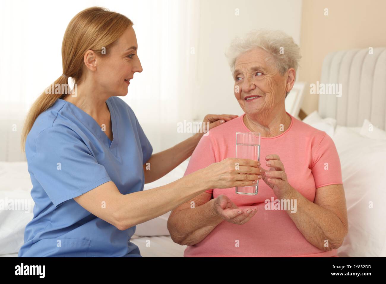 Healthcare worker giving glass of water to senior patient at home Stock ...