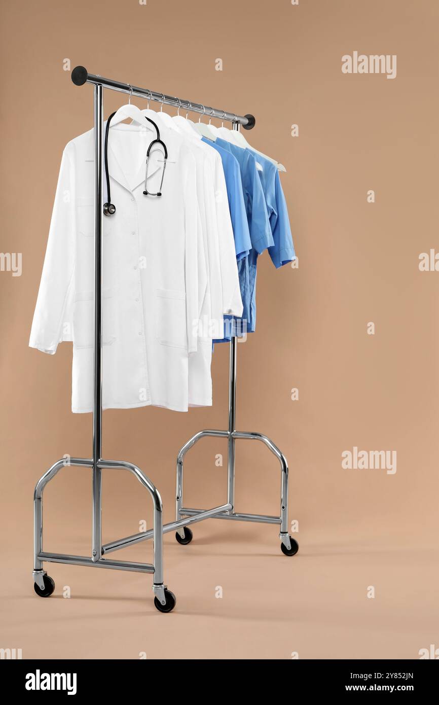 Different medical workers' uniforms and stethoscope on clothing rack ...