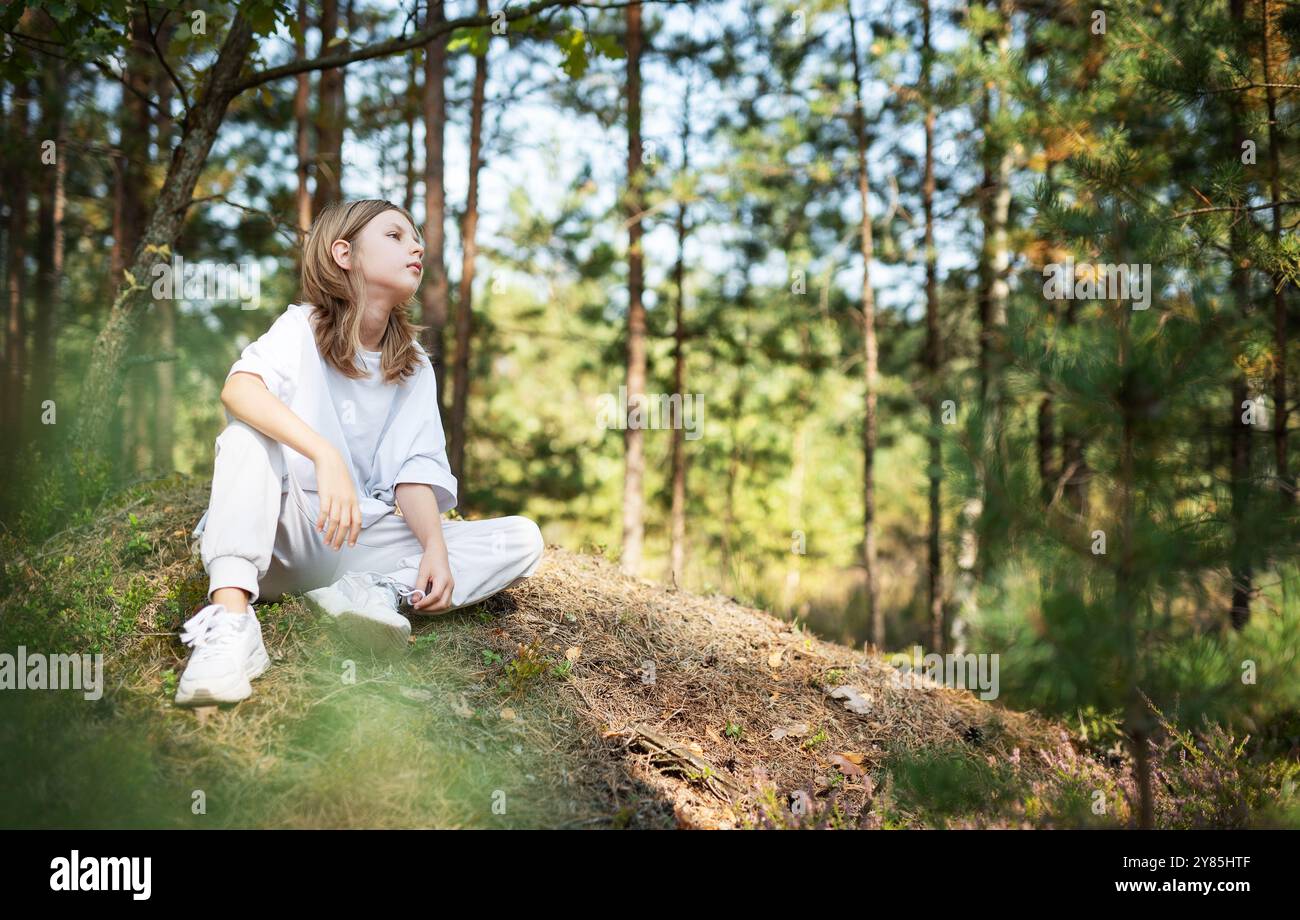 A young girl sits contentedly on a grassy slope in the forest ...