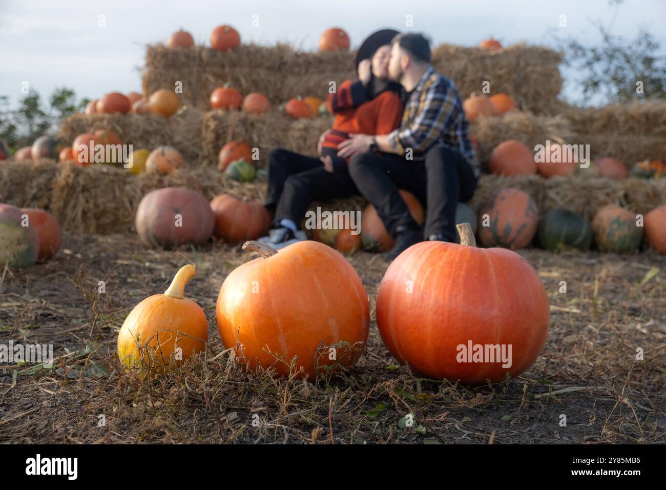 A couple sitting on hay bales surrounded by pumpkins in a pumpkin patch ...