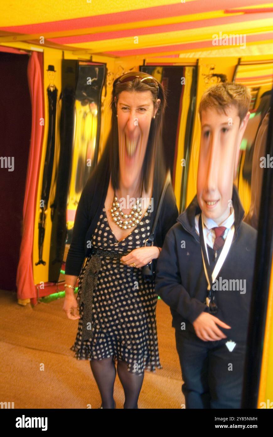 Funny distorting mirror. Mother and son looking into distorting mirror ...