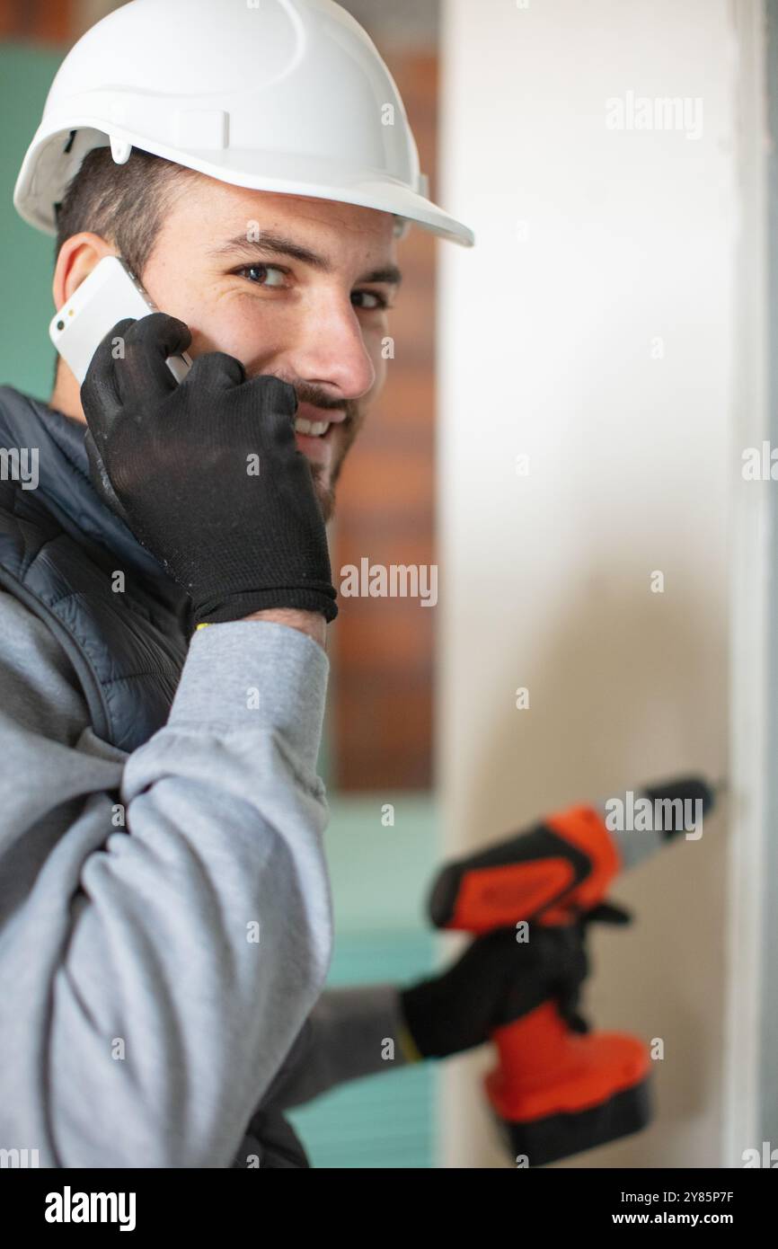 a tradesman using a cordless telephone while drilling wall Stock Photo ...