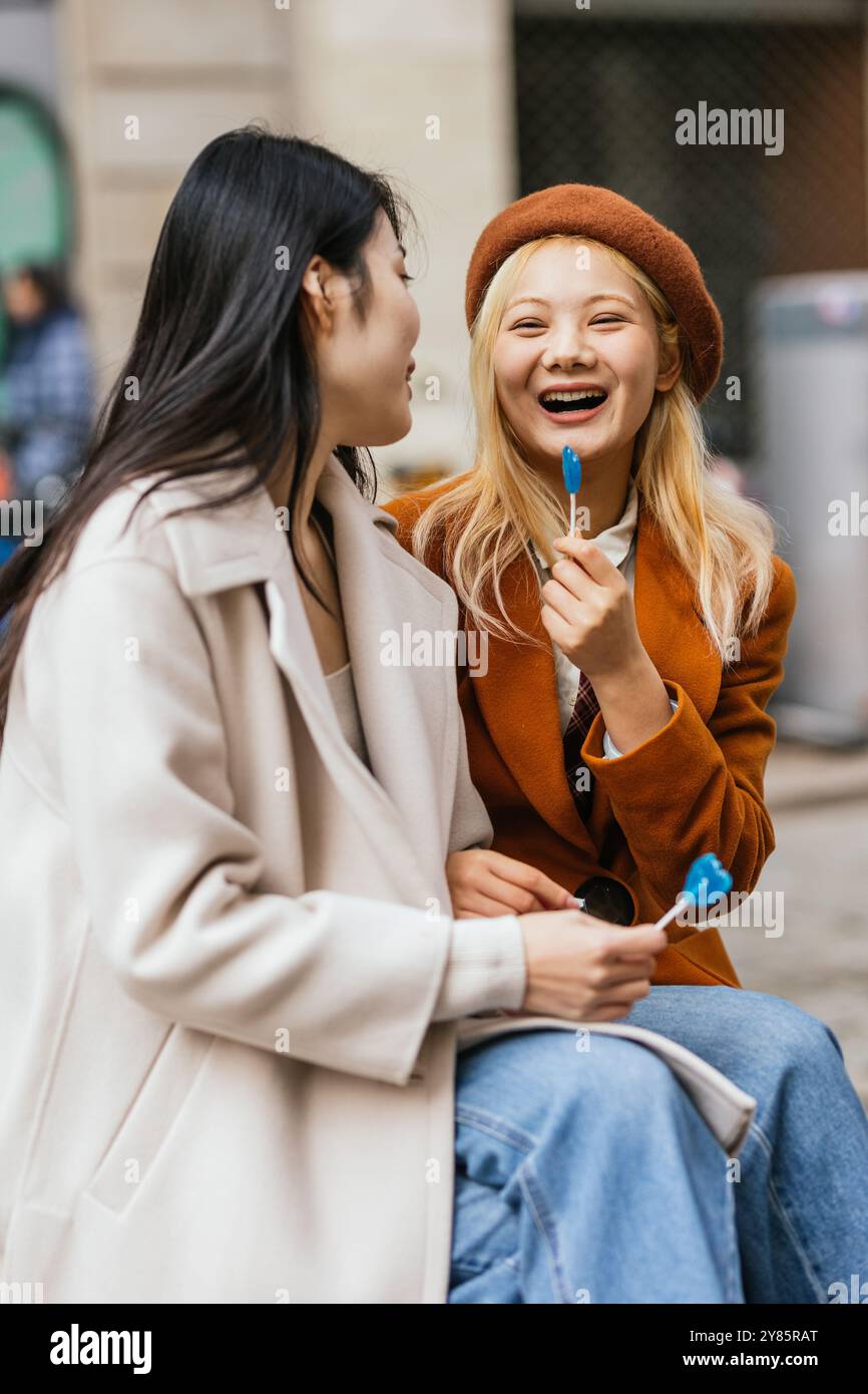 Two women sitting down, one with a bluelollipop in her mouth and the ...