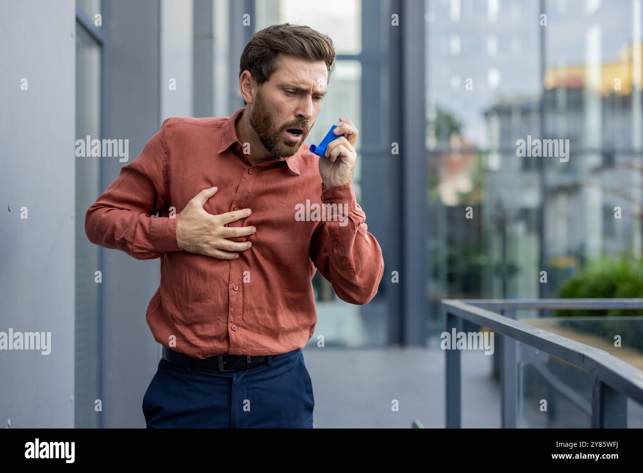 A man in an orange shirt is holding a blue inhaler. He is breathing ...