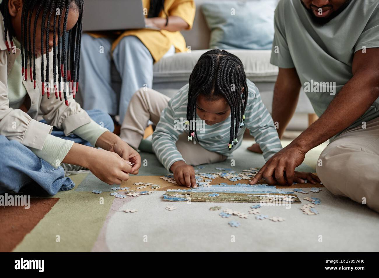 Two children and two adults sitting on floor engaged in solving large ...