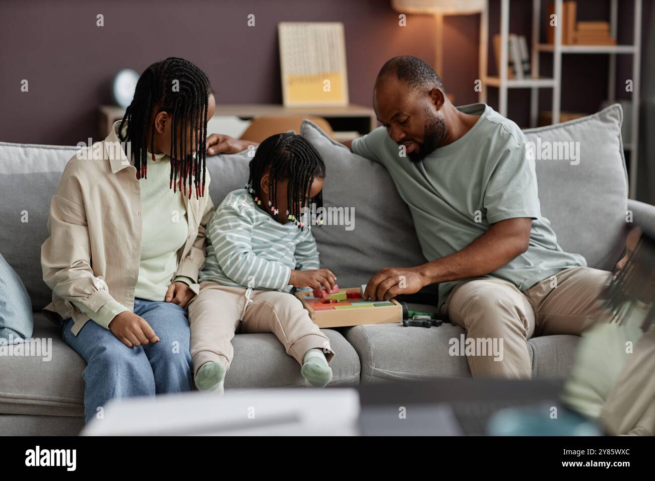 African American family interacting on sofa while playing educational ...