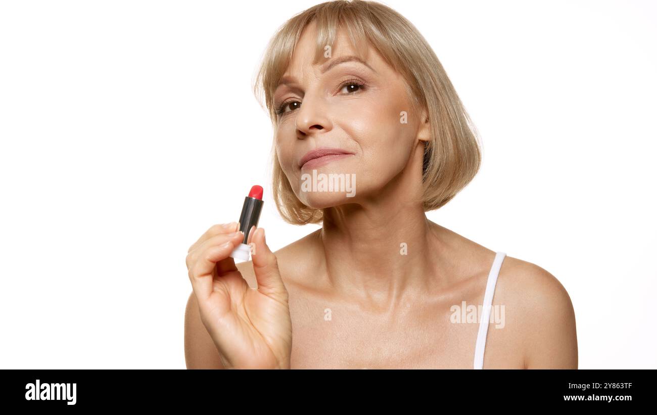 Mature woman holds lipstick confidently, ready to apply it, showing ...