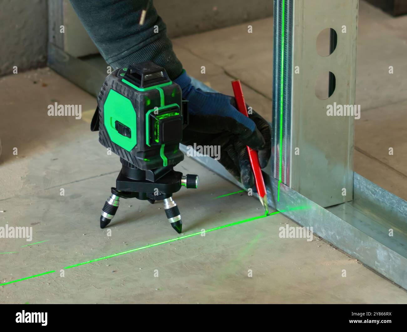 Construction worker using a cross line laser level and marking a red ...
