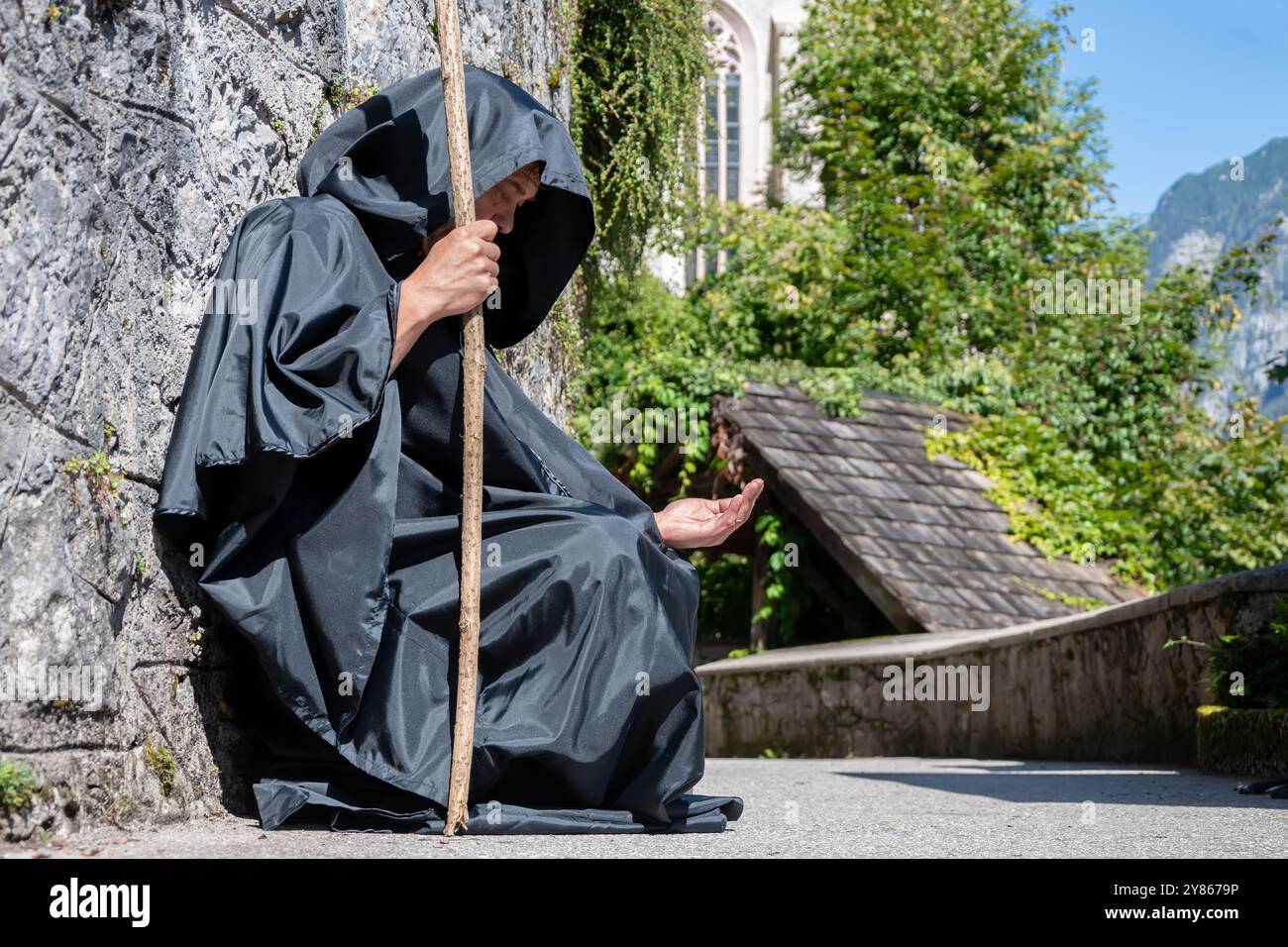 A monk in a black robe asks for alms with his hand outstretched ...