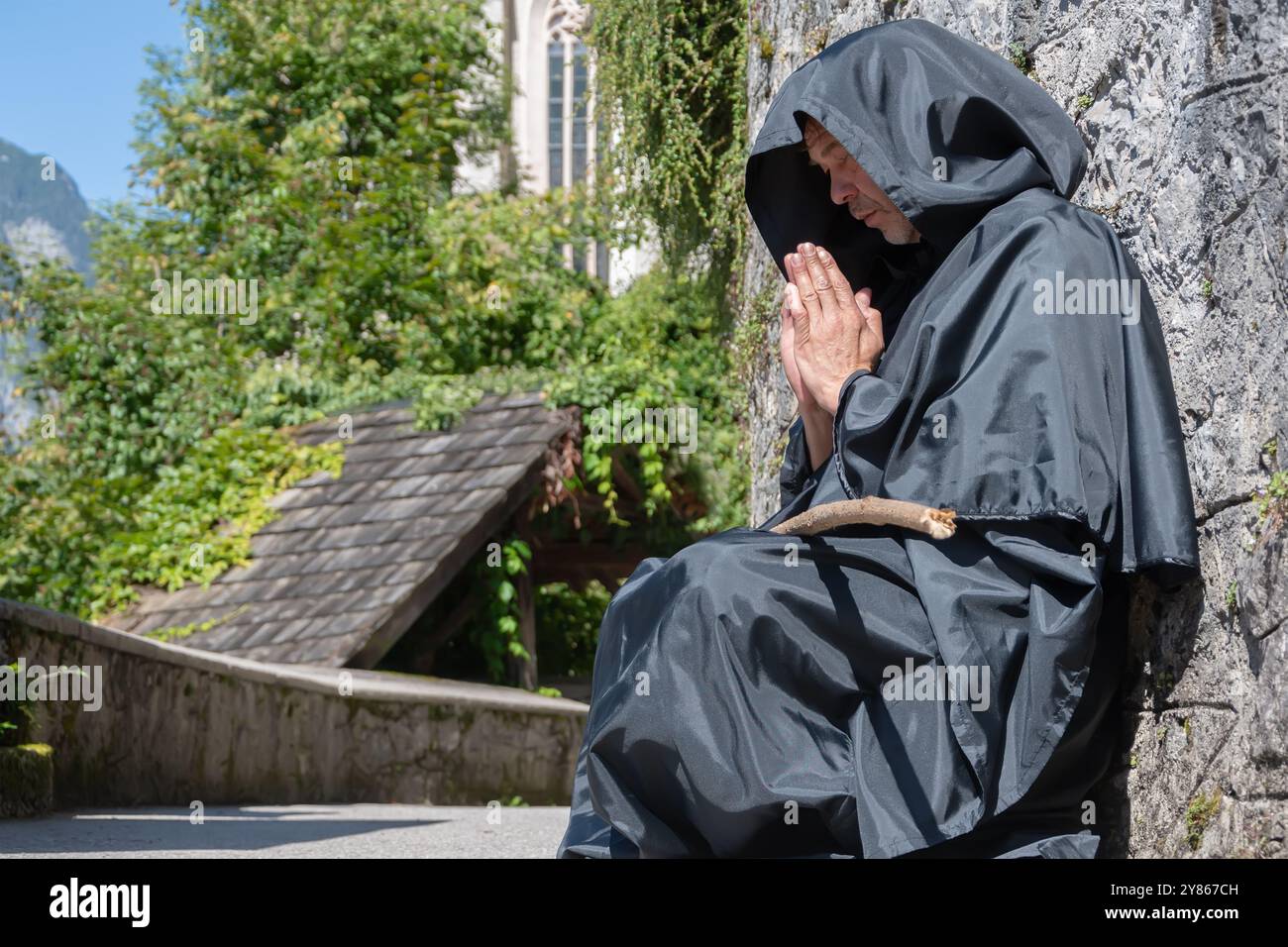 An old monk in a black cassock and carrying a staff is praying with his ...
