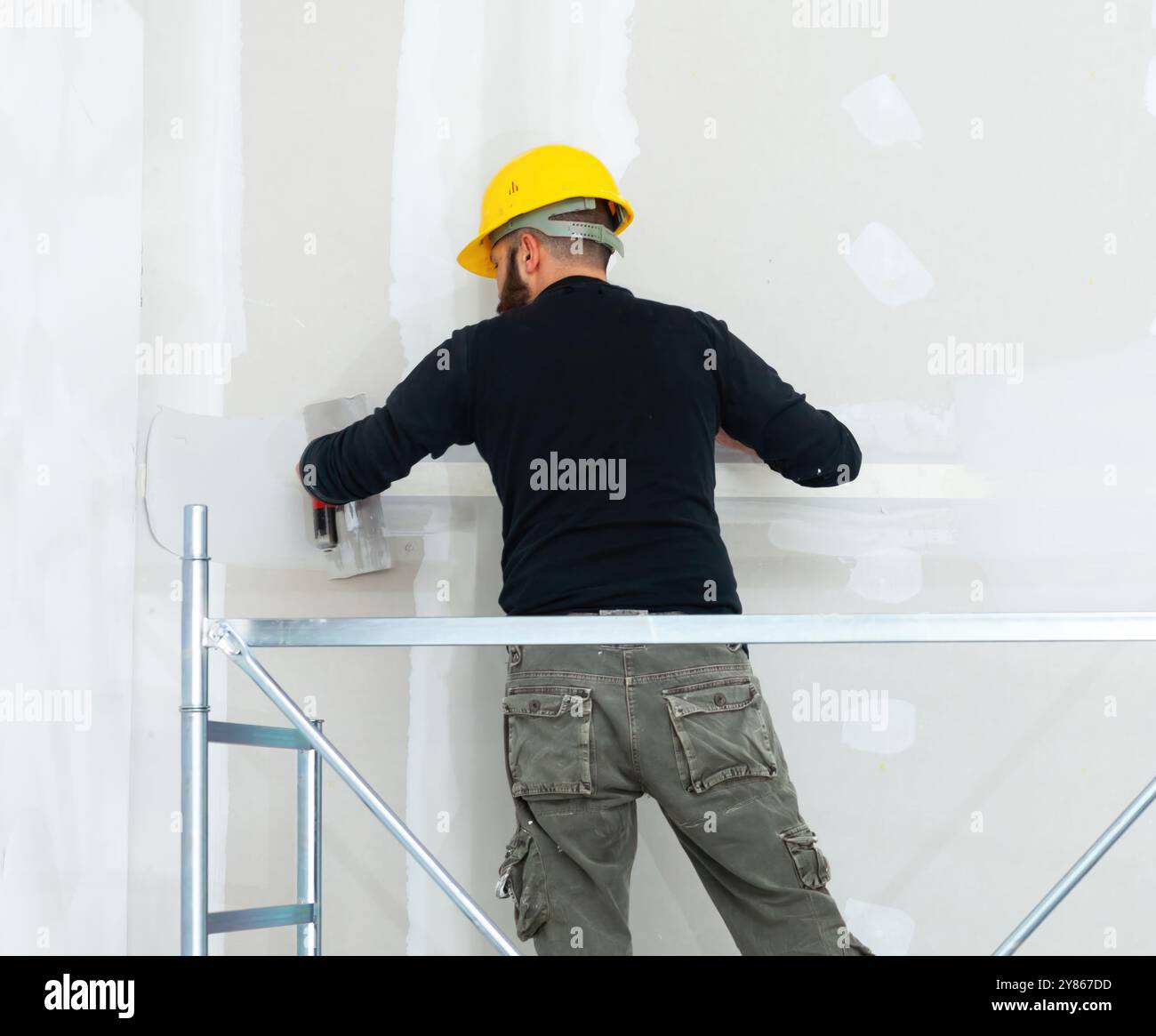 Construction worker wearing a hard hat and safety equipment plastering ...