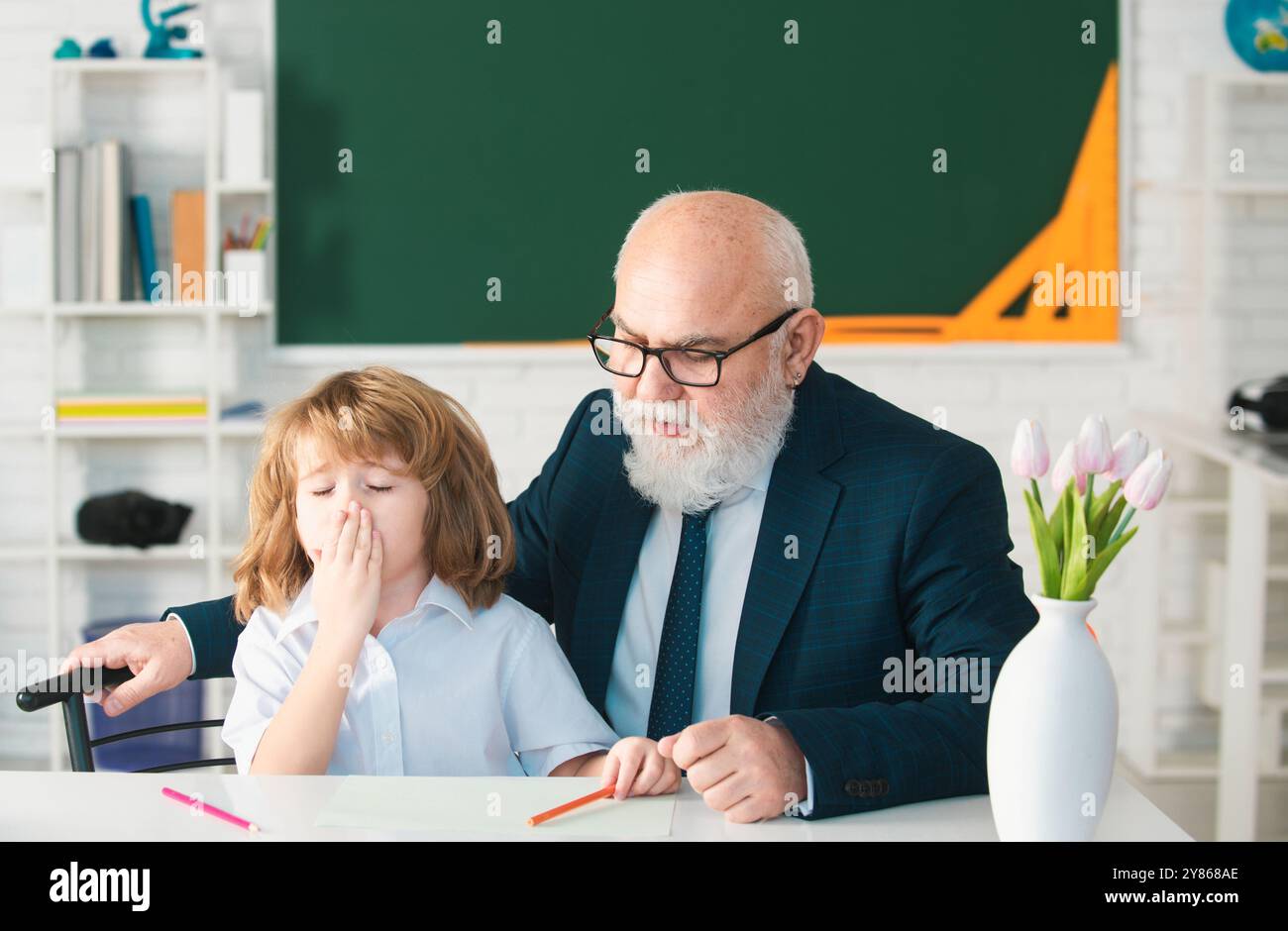 Help to learn. Old learner with schoolboy in classroom. School teacher ...