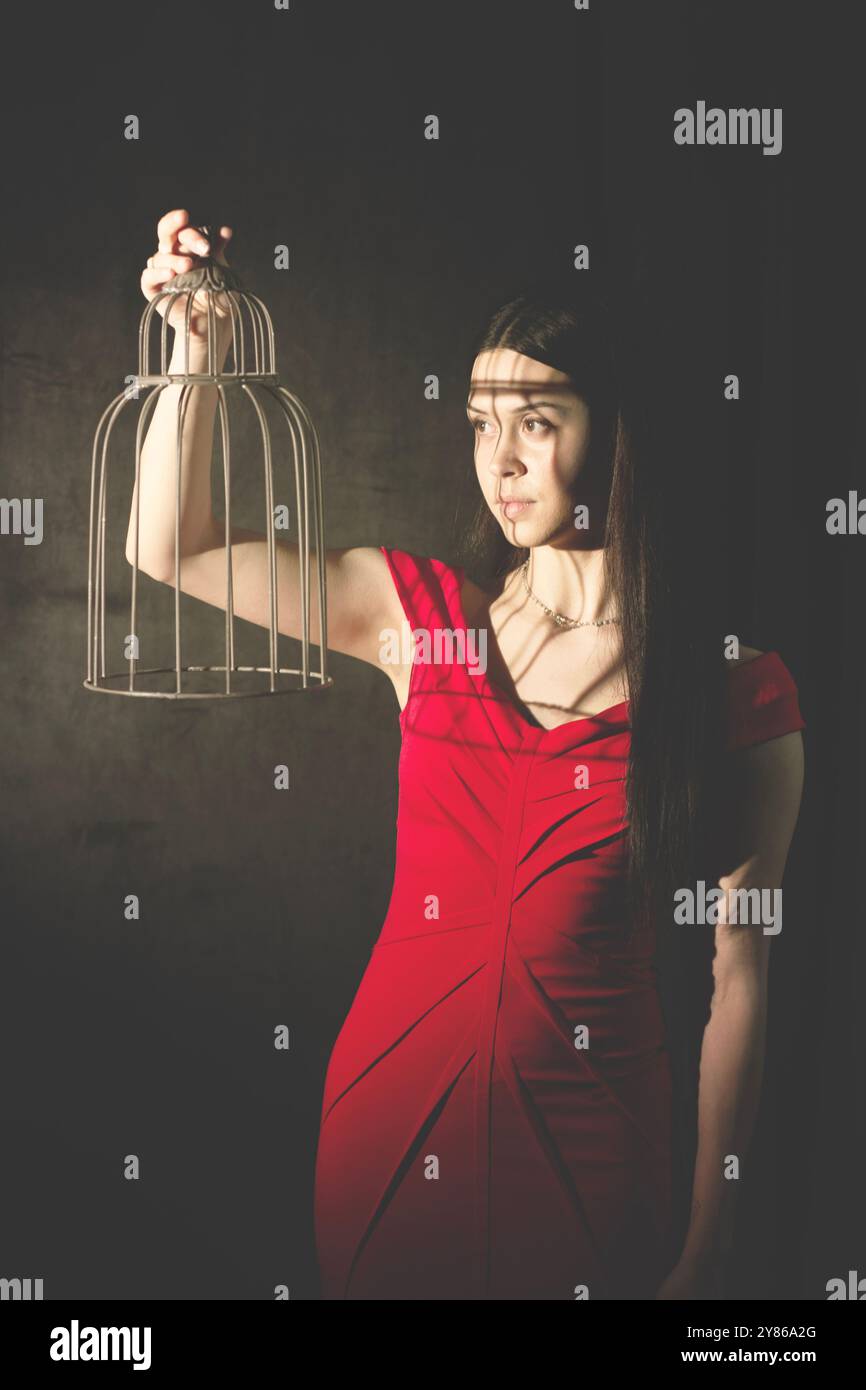 woman holding an empty cage with the reflection of the bars on her face ...
