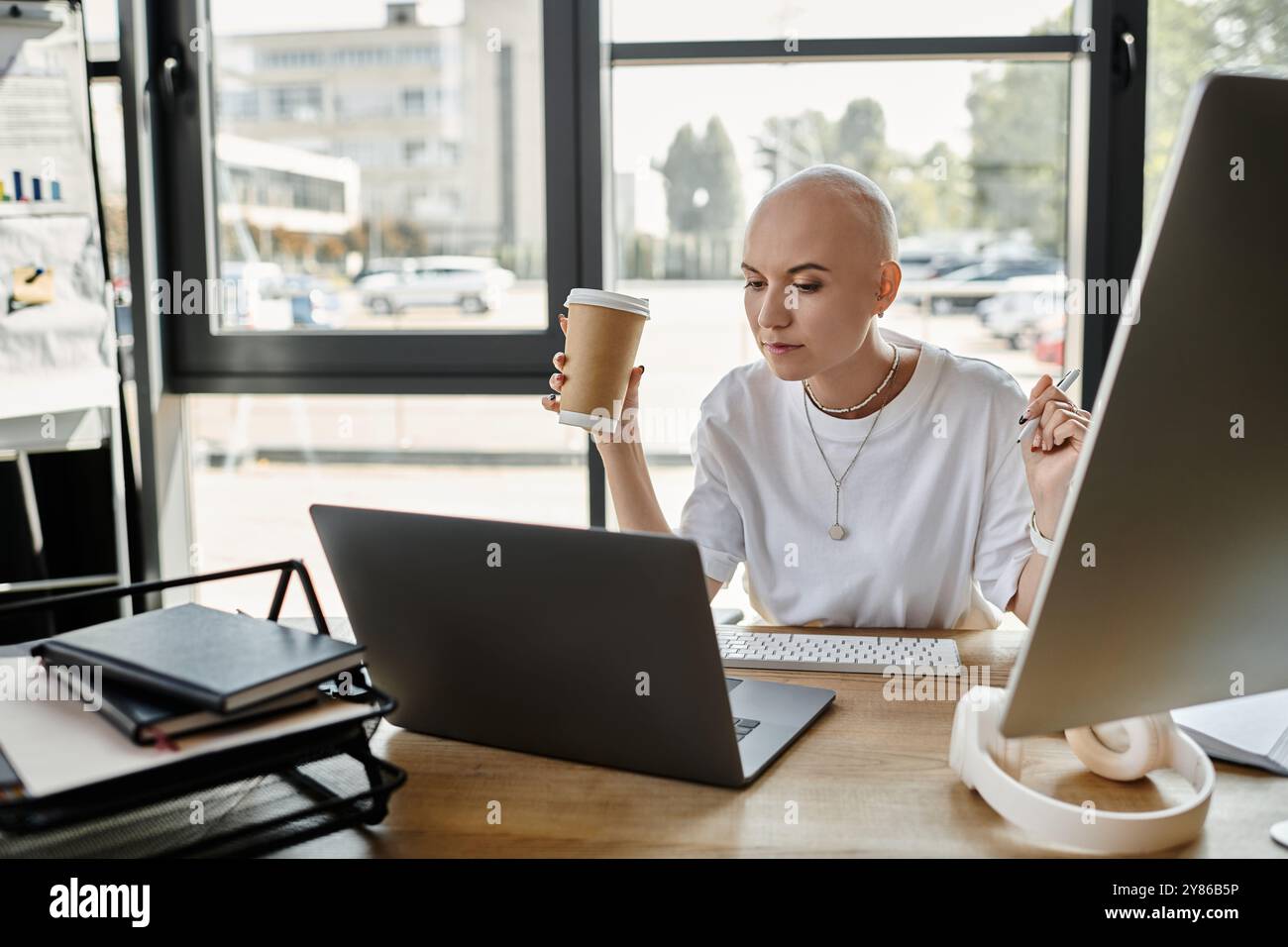 A young bald woman sips coffee while engaging with her laptop in a ...